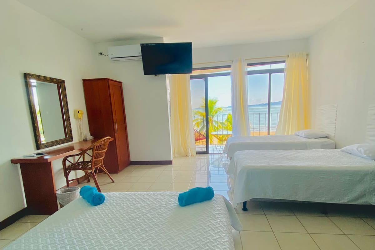 Quarto de hotel com duas camas, uma mesa de trabalho com cadeira, televisão e uma janela grande com cortinas.