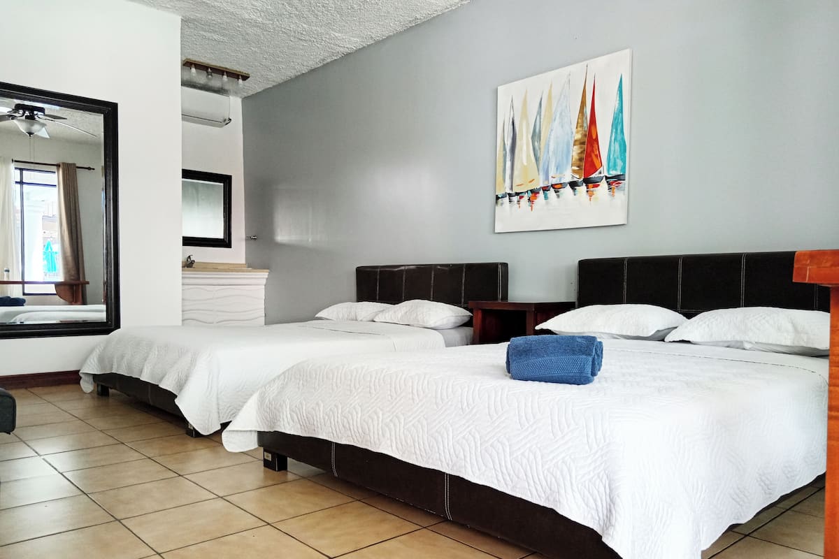 Quarto de hotel com duas camas, um espelho grande, uma pintura de barcos à vela e piso de azulejos.