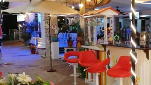 Uma área de bar com cadeiras vermelhas, um balcão com diversos itens e um letreiro que diz "HOM STORY BEGINS".