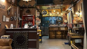 Um café acolhedor e bem iluminado, com decoração rústica, apresentando um balcão, área de estar e diversos artigos expostos.