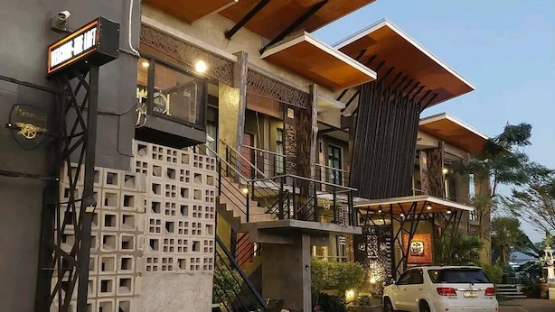 Um edifício moderno de dois andares com um grande beiral de madeira, entrada com portão e um carro branco estacionado em frente.