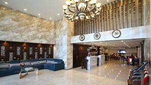 Um hall amplo com piso de mármore, um sofá azul, um candelabro e um balcão de recepção.