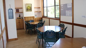 Uma sala de jantar com uma mesa e cadeiras de madeira, uma parede de tijolos, uma janela e um mural com avisos.