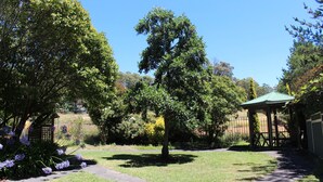 Um jardim com um caminho pavimentado, um gazebo e uma área cercada com árvores.