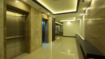 Corredor moderno de hotel com piso de mármore, um elevador e um banco ao longo da parede.