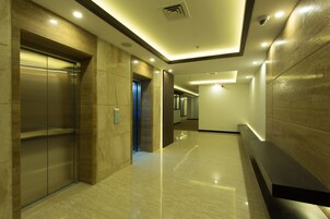 Corredor moderno de hotel com piso de mármore, um elevador e um banco ao longo da parede.