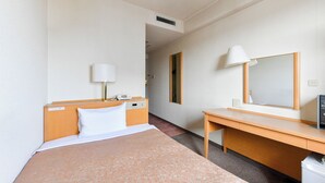 Quarto de hotel com cama, mesa de cabeceira, luminária e escrivaninha com espelho.