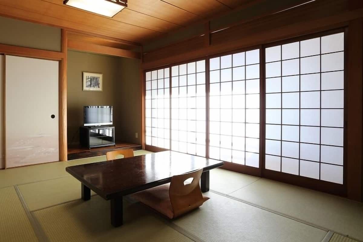 Um quarto japonês tradicional com tatames, uma mesa baixa, portas deslizantes e uma janela grande com biombos shoji.