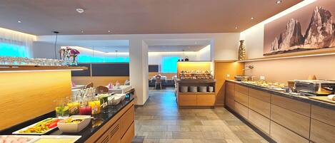 Espaço de café da manhã de um hotel moderno, com serviço de buffet, incluindo diversos alimentos e bebidas.
