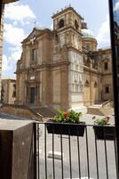 Um edifício histórico com uma cúpula imponente e um campanário, apresentando uma escadaria monumental que leva à entrada.