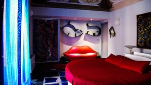 Quarto com colcha vermelha, um espelho grande e uma cadeira vermelha singular.