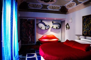 Quarto com colcha vermelha, um espelho grande e uma cadeira vermelha singular.