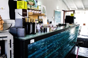 Uma área de bar com balcão de vidro, garrafas e diversos utensílios.