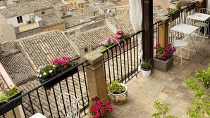 Uma varanda com pérgola, plantas em vasos e vista para uma cidade histórica com telhados de terracota.