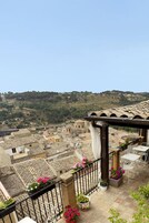 Uma varanda com pérgola, plantas em vasos e vista para uma cidade histórica com telhados de terracota.