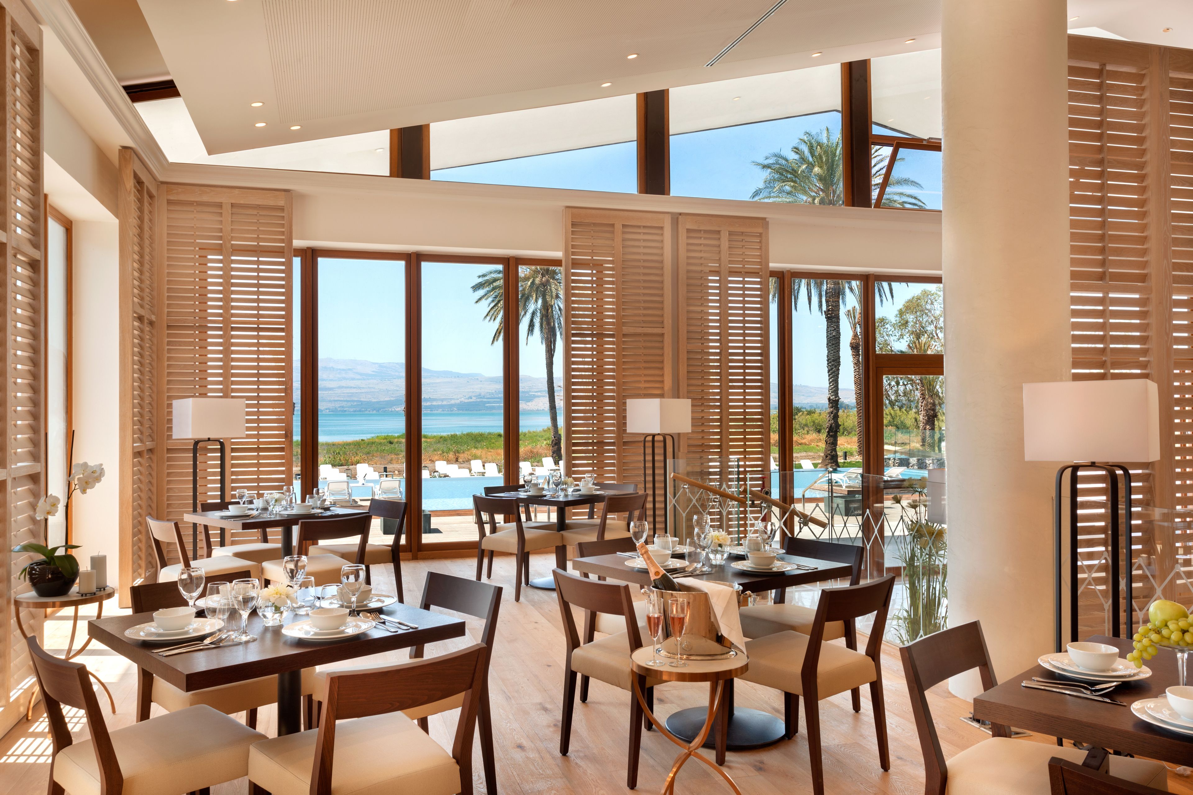 Uma sala de jantar com mesas preparadas para hóspedes, grandes janelas com vista para o oceano e um design de interiores moderno.