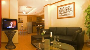 Uma sala de estar com televisão, sofá, mesa de centro com um vaso e taças de champanhe, e um espaço de jantar com cadeiras e mesa.