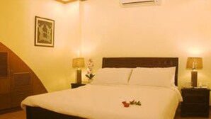 Quarto de hotel com uma cama grande, duas mesas de cabeceira com luminárias, um ar condicionado fixado na parede e um quadro emoldurado.