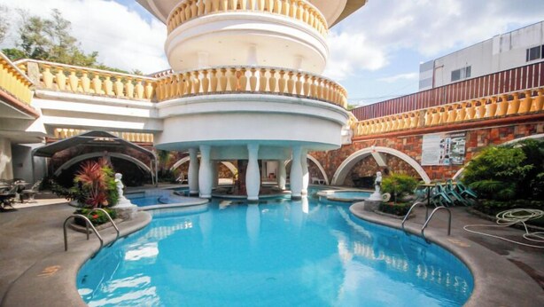 Uma área de piscina com uma fonte circular central, vários espaços de estar e uma seção coberta com telhado curvo.