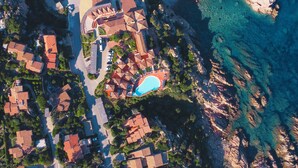 Vista aérea de uma propriedade costeira com piscina, casas em terraços e falésias rochosas.