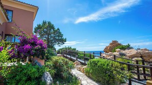 Uma trilha de pedra leva a um deck de madeira com vista para a costa rochosa.
