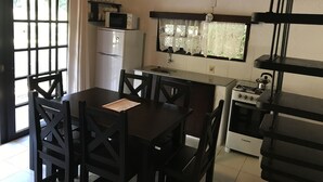 Uma cozinha compacta com geladeira, micro-ondas, fogão e uma janela com cortinas de renda.