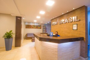 Uma receção com a placa "BEM BRASIL", uma planta em vaso e um certificado emoldurado na parede.