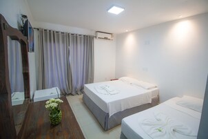 Quarto de hotel com duas camas, uma mesa de madeira com um vaso de flores, um espelho e uma janela com cortinas.