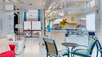 Um lobby de hotel moderno com um sofá vermelho, cadeiras azuis, um bar de café e vista para a cidade.