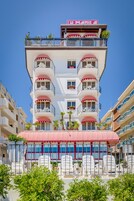 Um hotel com vários andares, varandas, toldos listrados em vermelho e branco e mesas ao ar livre.