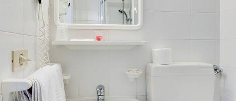Casa de banho com uma sanita, lavatório branco, espelho com luzes e secador de cabelo.
