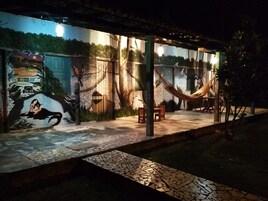 Uma área externa com assentos, um mural, uma rede e piso de azulejos.