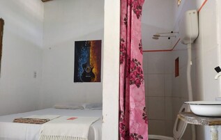 Quarto com cama, um quadro na parede, banheiro com pia, vaso sanitário e cortina de chuveiro.