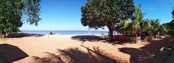 Uma praia com uma estrutura de colmo, palmeiras e barcos na água.