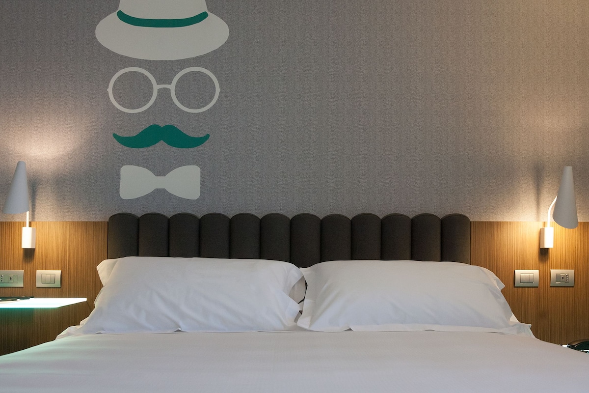 Quarto de hotel com uma cama grande, duas luminárias de cabeceira e uma parede com padrão.
