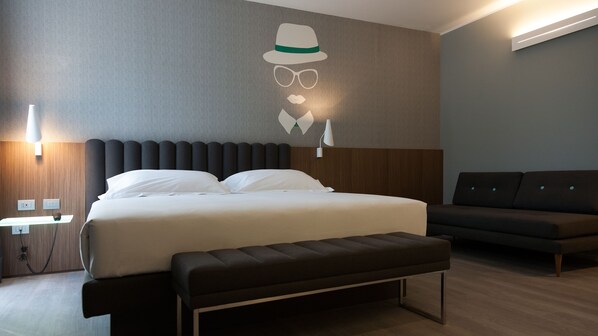 Quarto de hotel moderno com uma cama grande, um banco, um sofá e um aplique de parede.