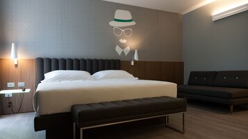 Quarto de hotel moderno com uma cama grande, um banco, um sofá e um aplique de parede.