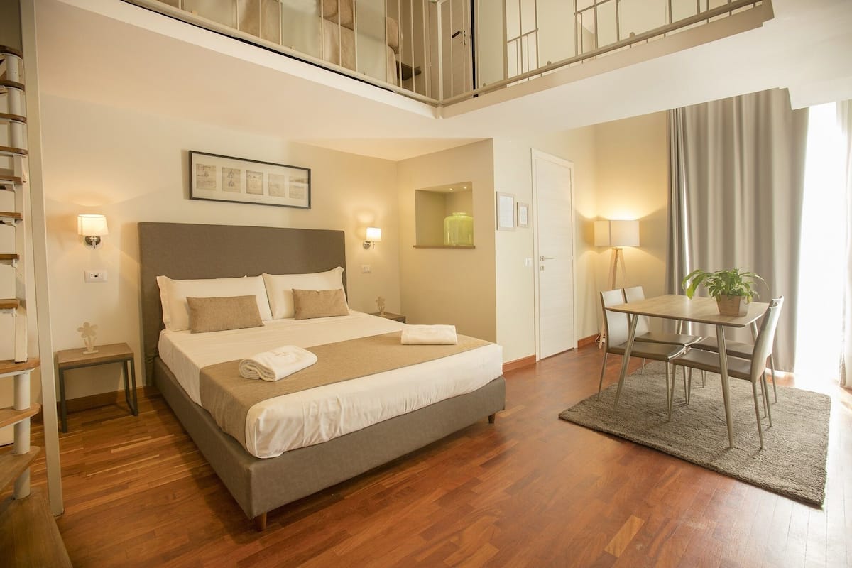 Quarto de hotel com cama, mesas de cabeceira, escrivaninha e cadeira.