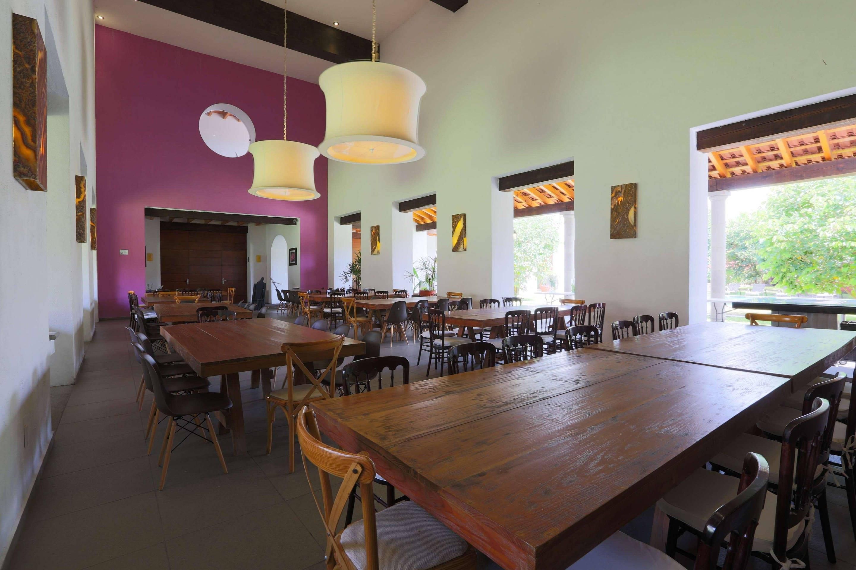 Uma sala de jantar ampla com várias mesas e cadeiras de madeira, luminárias pendentes grandes e obras de arte nas paredes.