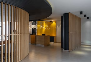 Uma área de recepção moderna com um painel de madeira curvo, balcão de recepção e área de estar.