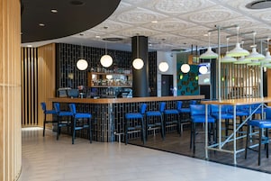 Uma área de bar moderna com balcão de madeira, banquetas azuis e teto estampado.
