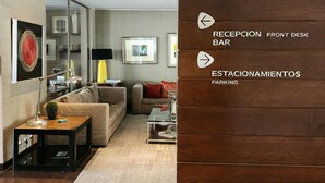 Um hall de hotel moderno com balcão de recepção, bar e área de estar com sofás e mesa de centro.