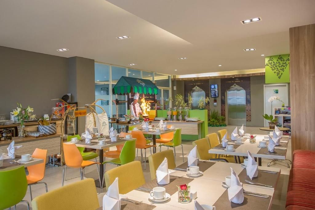 Restaurante moderno com várias mesas e cadeiras, um chef preparando comida e uma marquise verde.