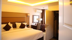 Quarto de hotel com cama, escrivaninha, cadeira, ar condicionado e porta.