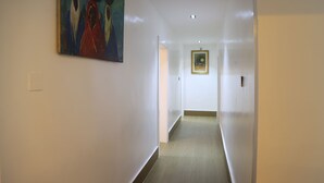 Um corredor com uma pintura na parede à esquerda, um quadro emoldurado na parede à direita e uma porta no final.