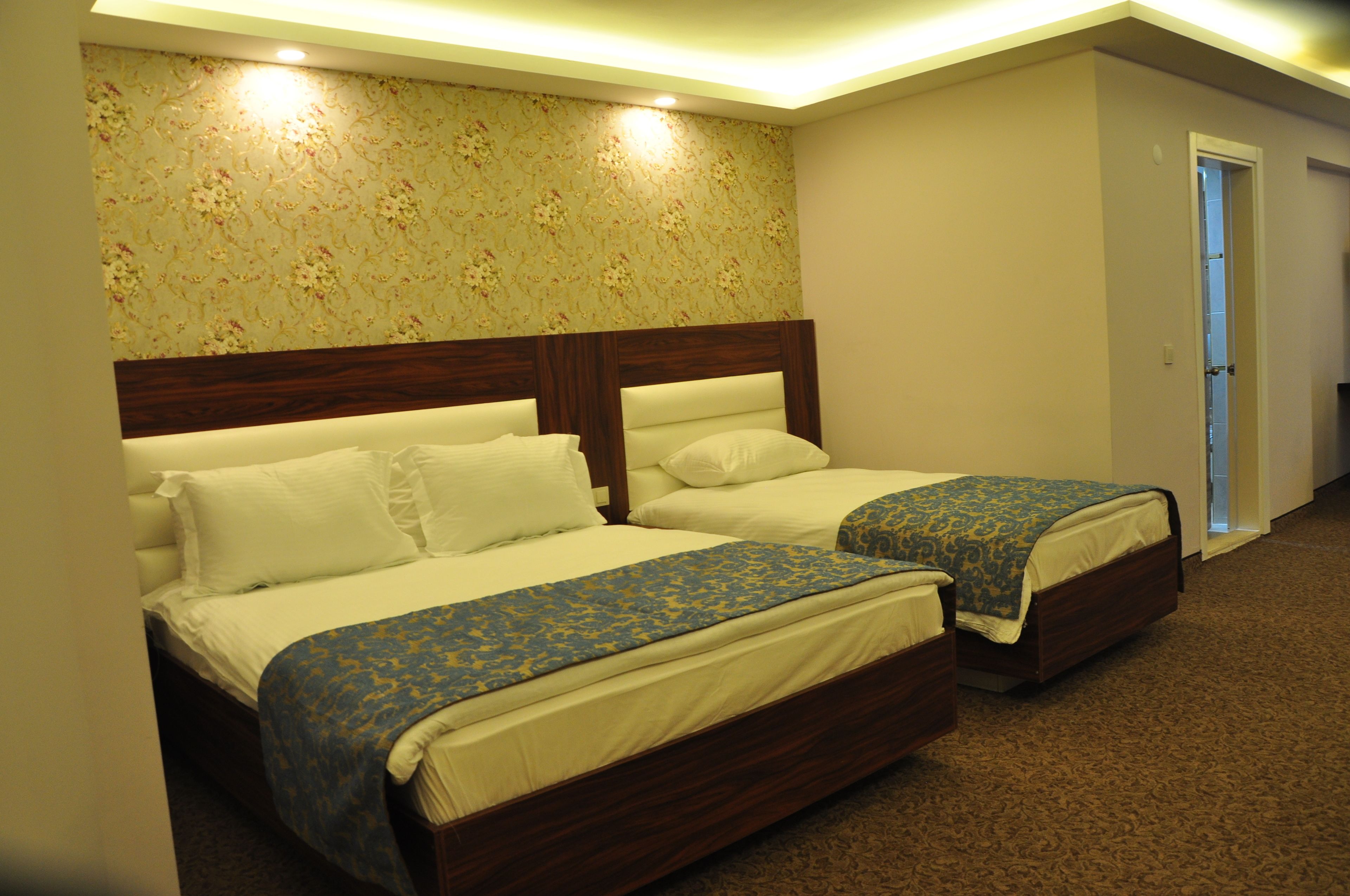 Quarto de hotel com duas camas, papel de parede floral e piso coberto por carpete.