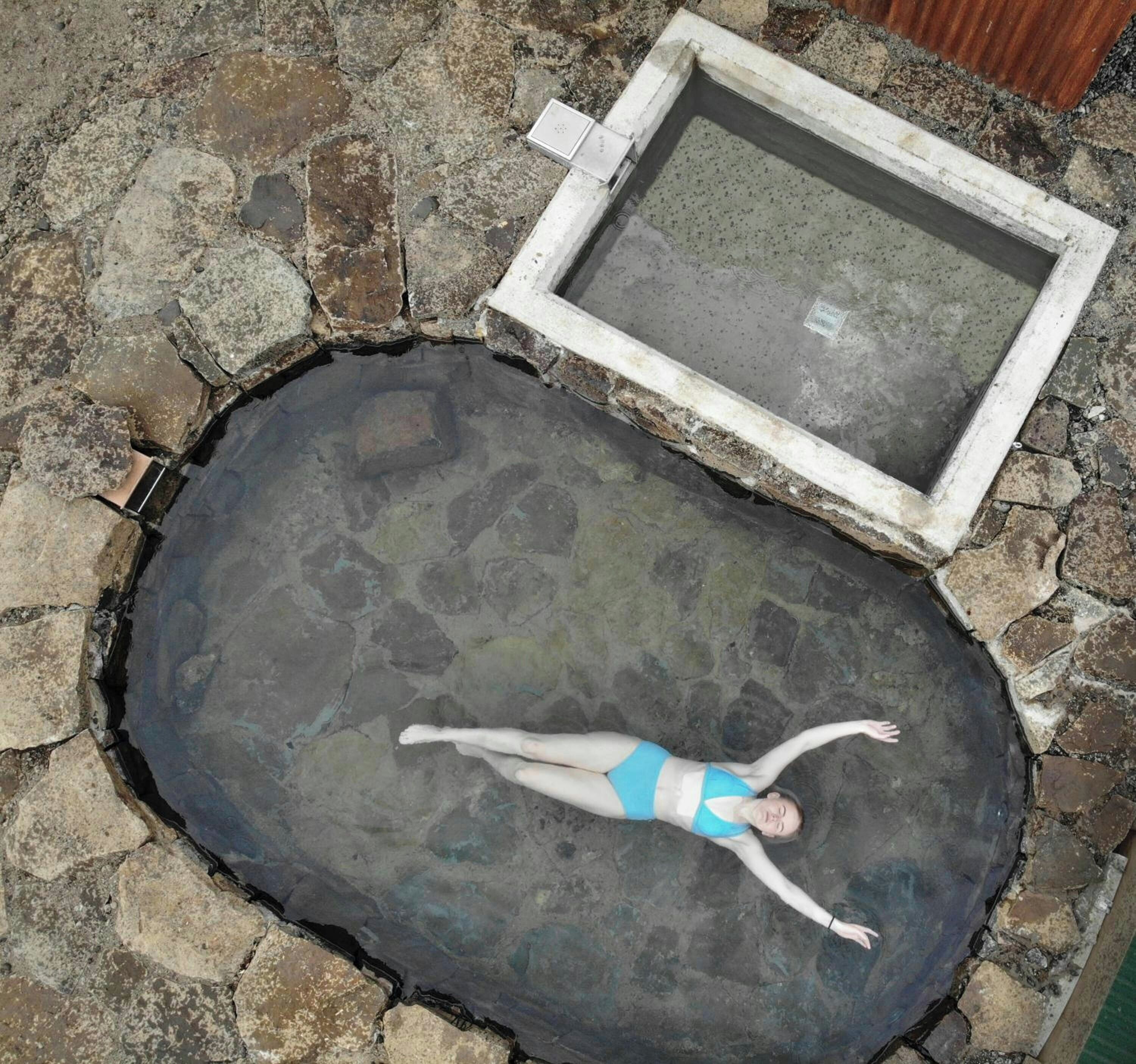 Uma pessoa deitada em uma superfície de pedra com uma piscina retangular ao lado.