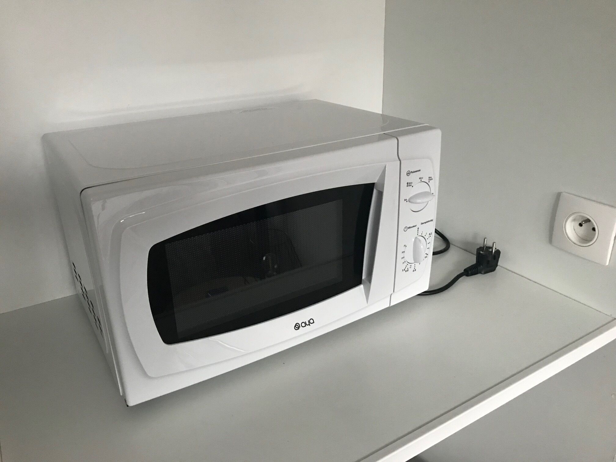 Um micro-ondas branco sobre uma bancada branca, com um cabo de alimentação conectado.