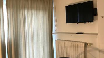 Quarto com cama, televisão na parede, radiador e janela com cortinas.