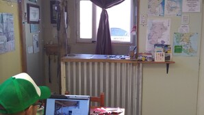 Um homem sentado à mesa de madeira usando um laptop num quarto com janela, vários papéis e mapas na parede.